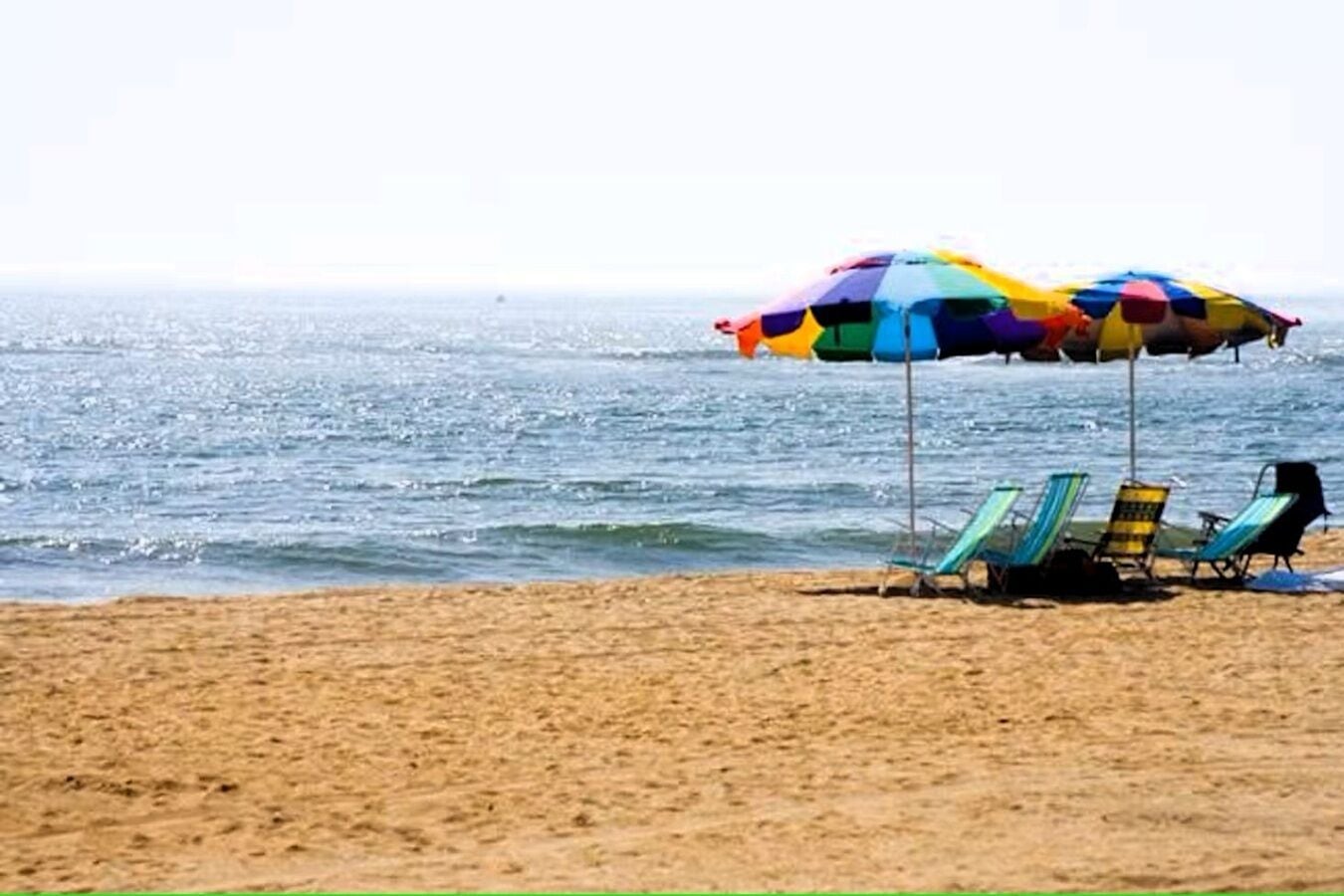 Uma praia com dois guarda-sóis coloridos e duas cadeiras de praia.