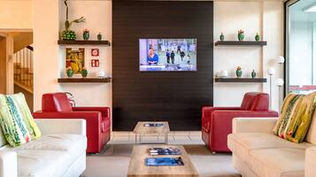 Uma sala de estar moderna com uma televisão de tela plana presa a uma parede escura, sofás de couro vermelho, uma mesa de centro de madeira e objetos decorativos em prateleiras.