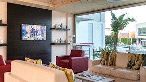 Um hall de hotel moderno com uma grande tela de TV, assentos confortáveis e vista para o exterior.