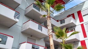 Um edifício de vários andares com varandas, algumas com guarda-corpos vermelhos.