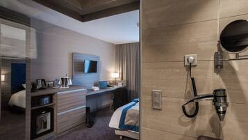 Quarto de hotel com cama, escrivaninha e área de chuveiro.