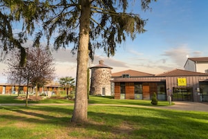 Um edifício com uma torre de pedra, uma entrada moderna e um jardim bem cuidado.