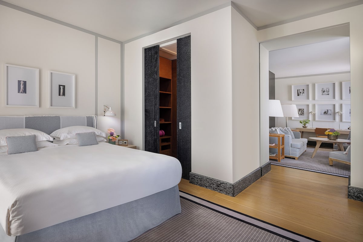 Quarto de hotel com uma cama grande, um guarda-roupa, uma mesa com cadeira e quadros nas paredes.