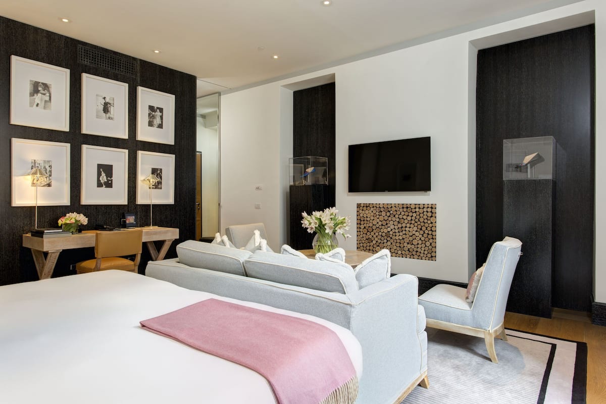Quarto de hotel moderno com uma cama grande, um sofá, uma escrivaninha e uma TV fixada na parede.
