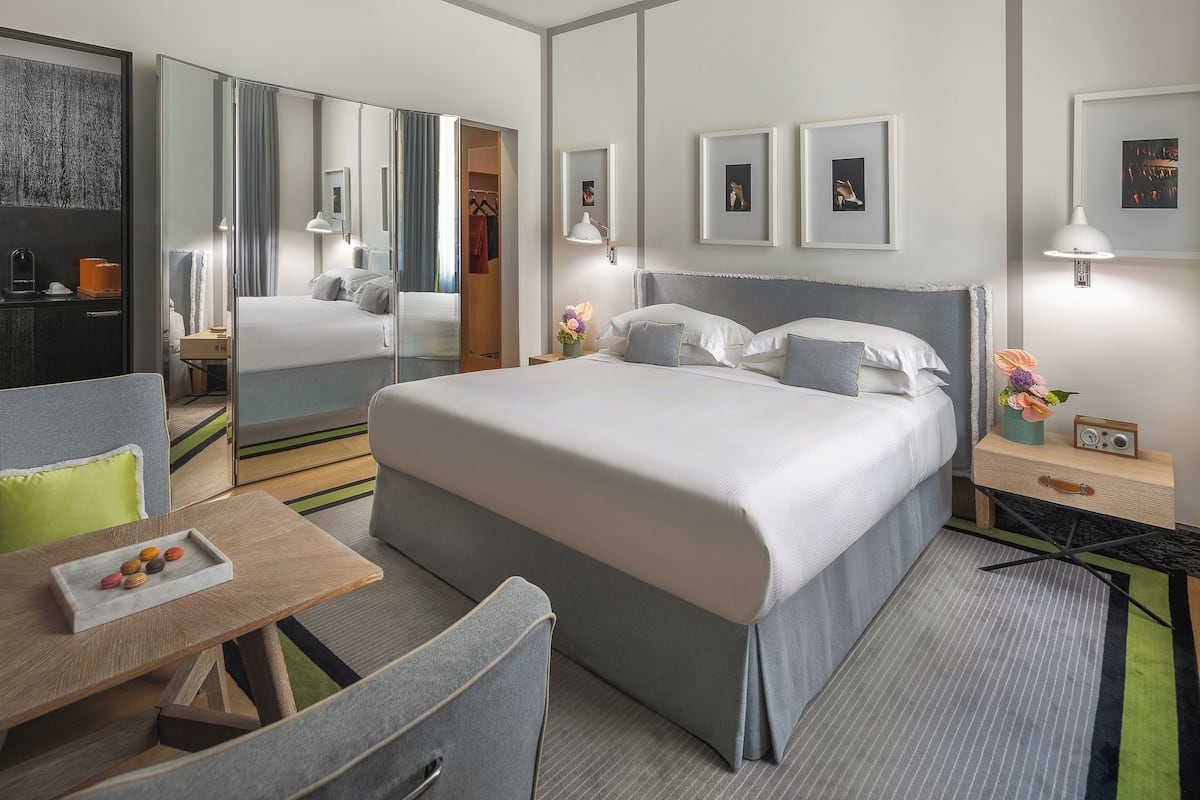 Quarto de hotel com cama grande, mesas de cabeceira, escrivaninha e uma cadeira, e espelho.