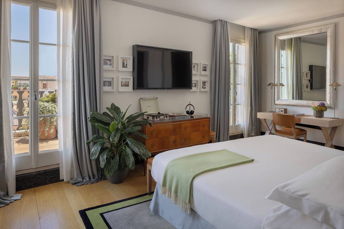 Quarto de hotel com uma cama grande, televisão de tela plana, cômoda, escrivaninha e uma janela ampla com cortinas.