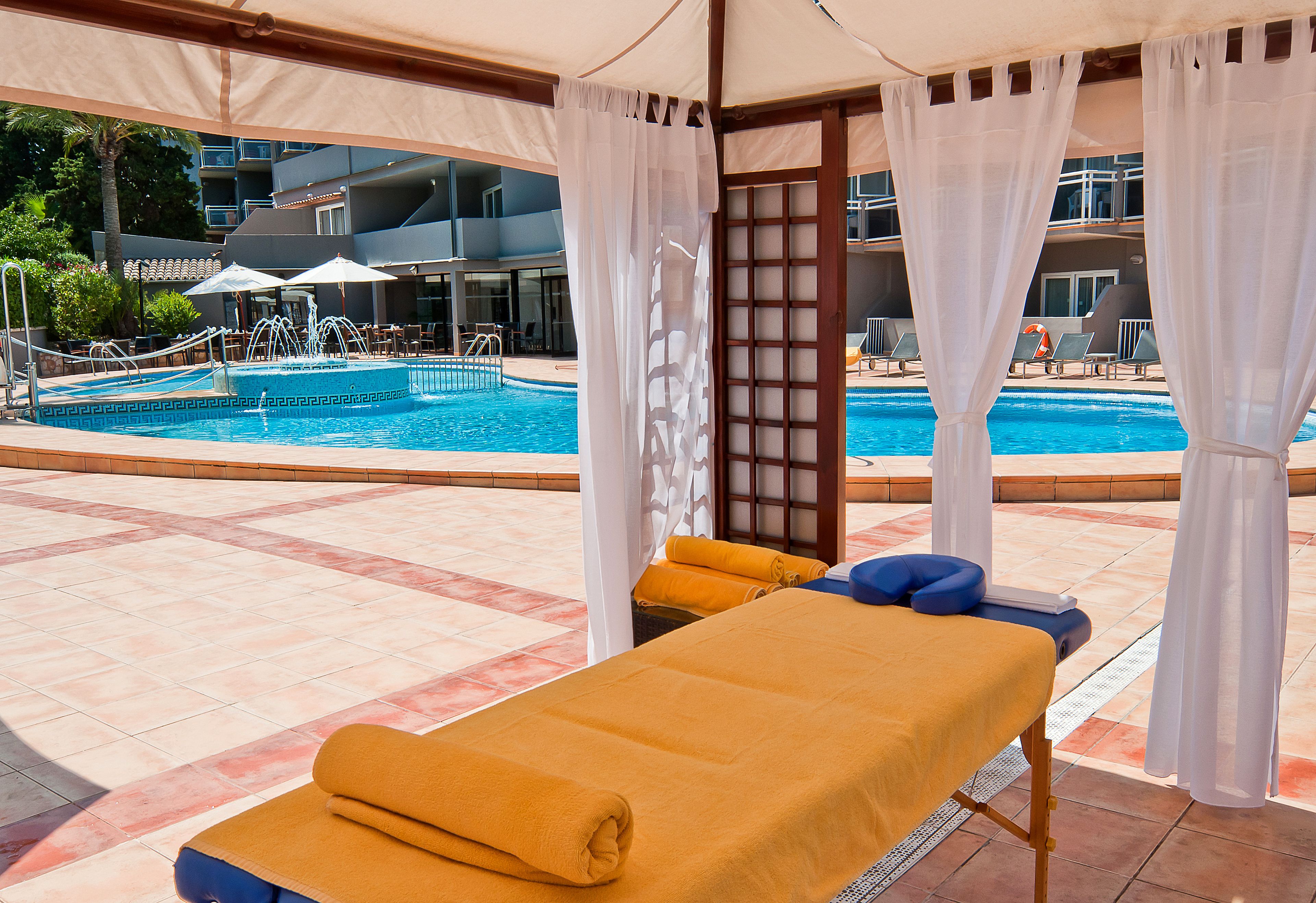Uma espreguiçadeira com uma toalha, uma piscina e um edifício ao fundo.