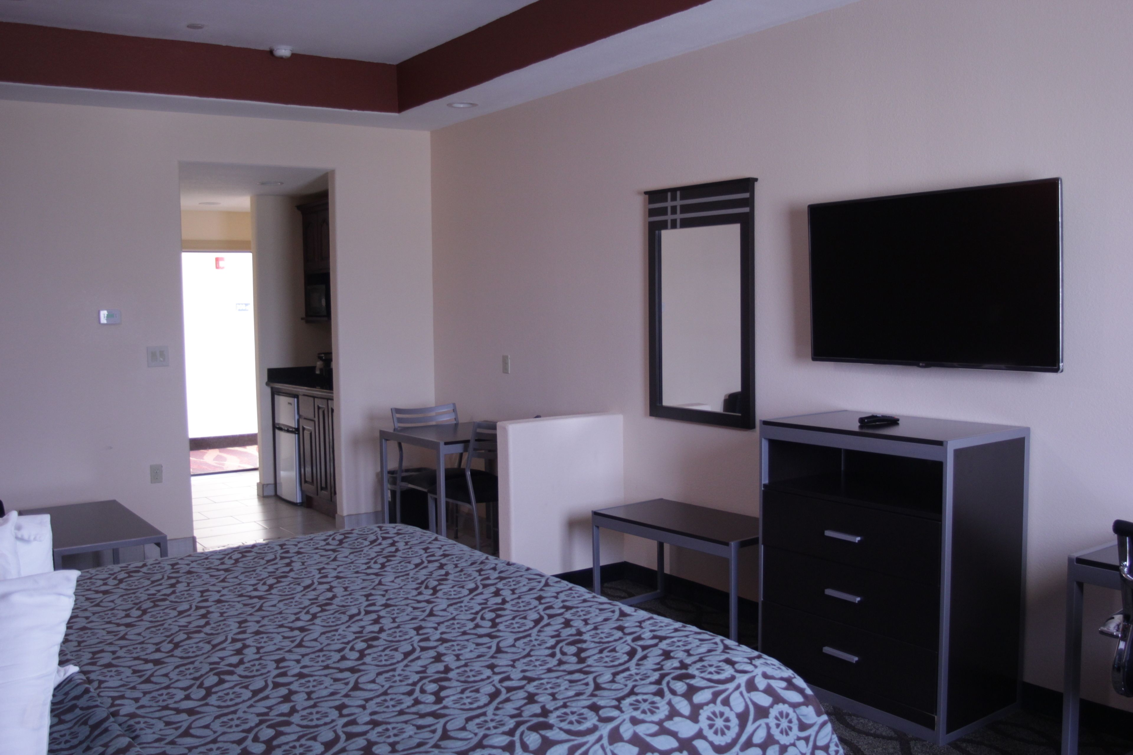 Quarto de hotel com cama, escrivaninha, cadeira, cômoda e televisão na parede.