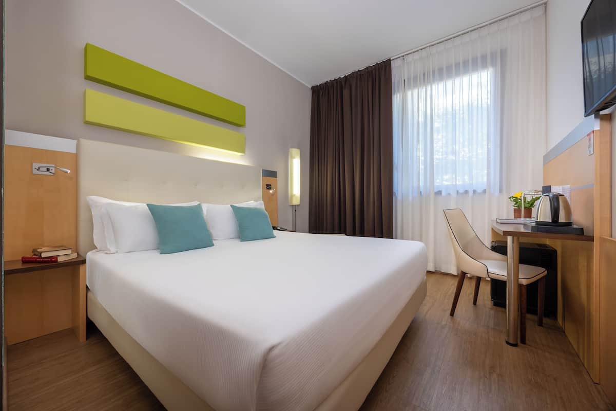 Quarto de hotel com uma cama grande, uma mesa, uma cadeira e uma televisão.