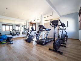 Uma academia moderna com diversos aparelhos de cardio, um espelho grande e piso de madeira.