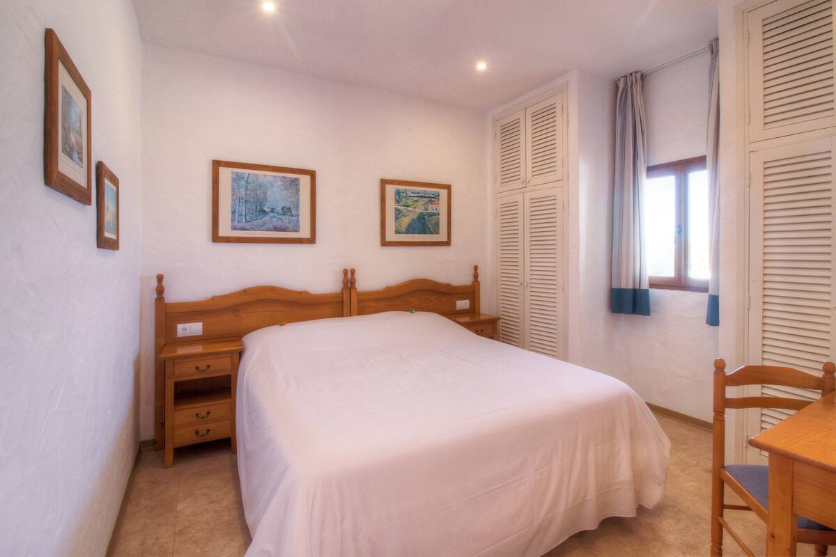 Um quarto com uma cama de solteiro, uma mesa de cabeceira de madeira, uma cadeira e uma janela com persianas.