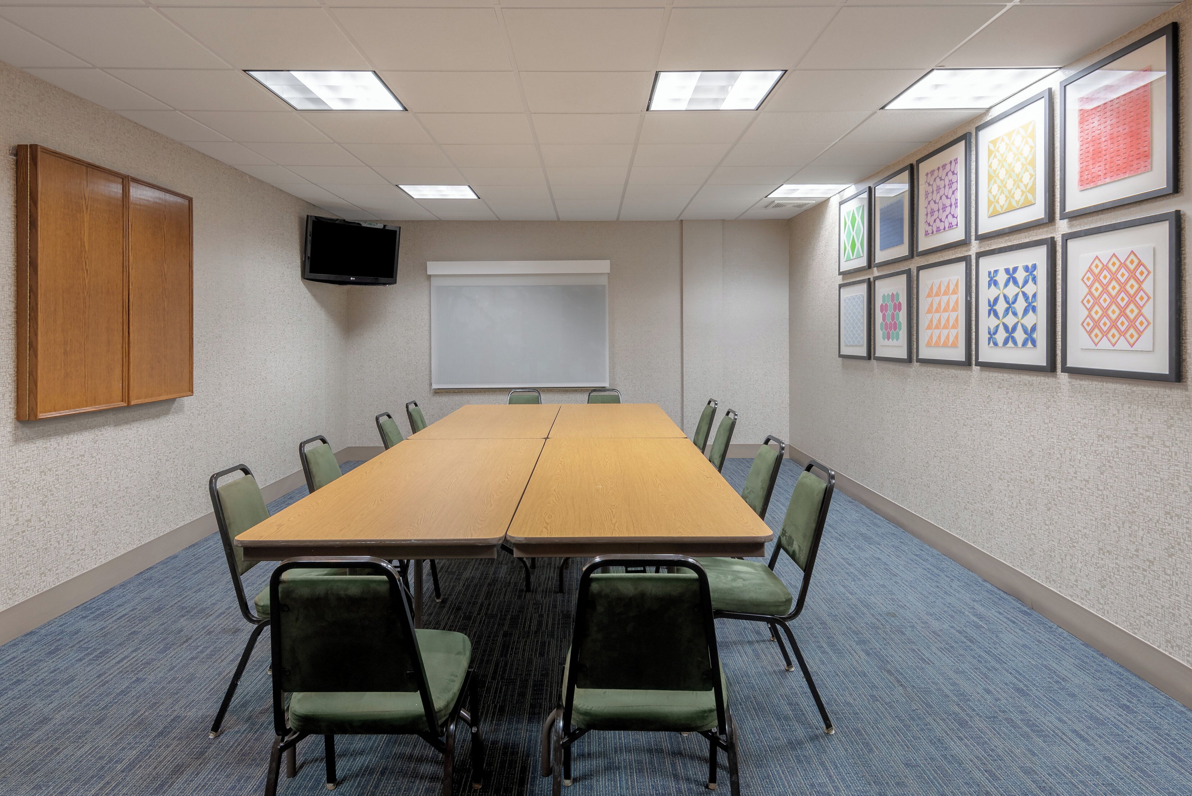 Uma sala de conferências com uma mesa comprida, cadeiras, uma tela de projetor e quadros nas paredes.