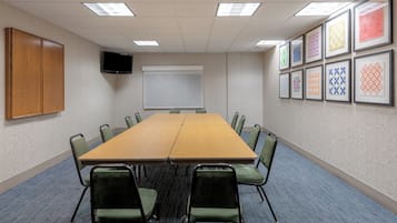 Uma sala de conferências com uma mesa comprida, cadeiras, uma tela de projetor e quadros nas paredes.