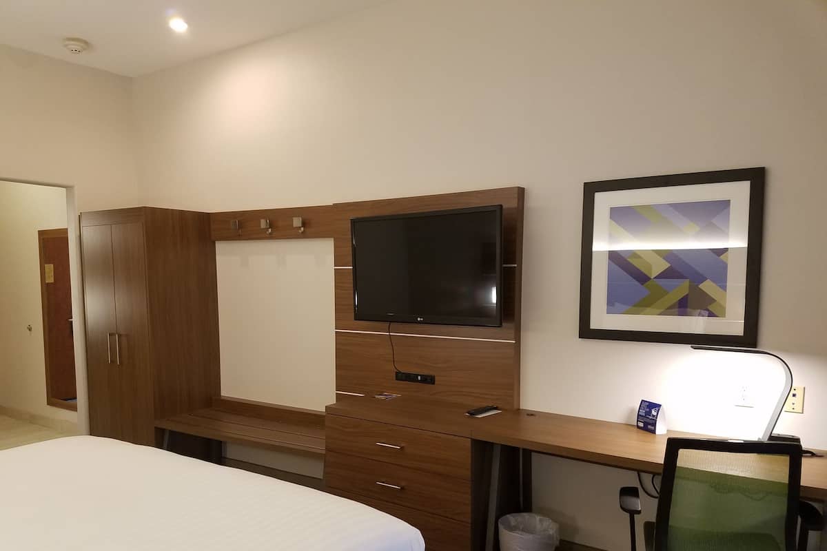 Quarto de hotel com uma cama, uma escrivaninha com computador, televisão e um quadro na parede.