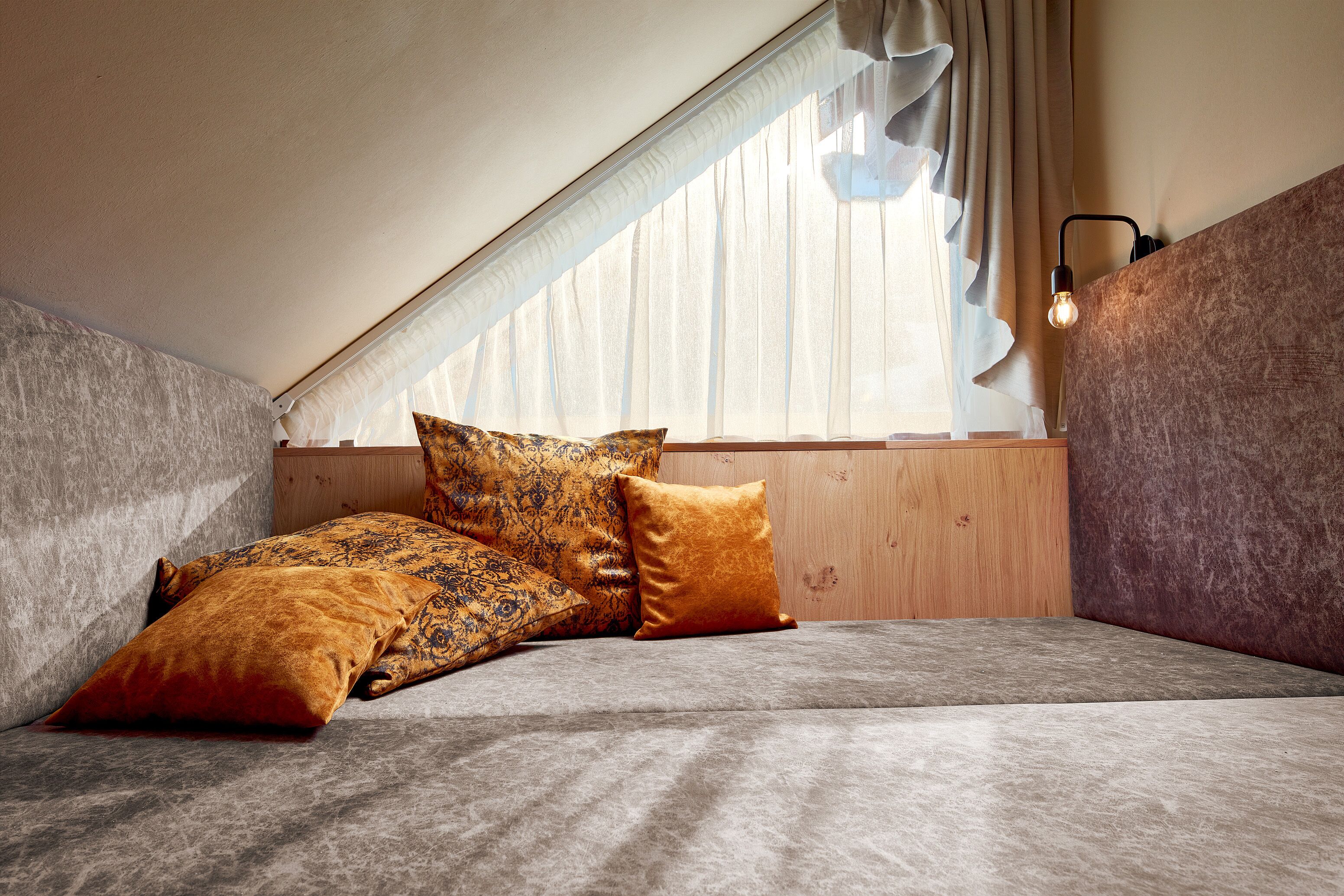 Um quarto aconchegante com cama, janela com cortinas e luminária na parede.