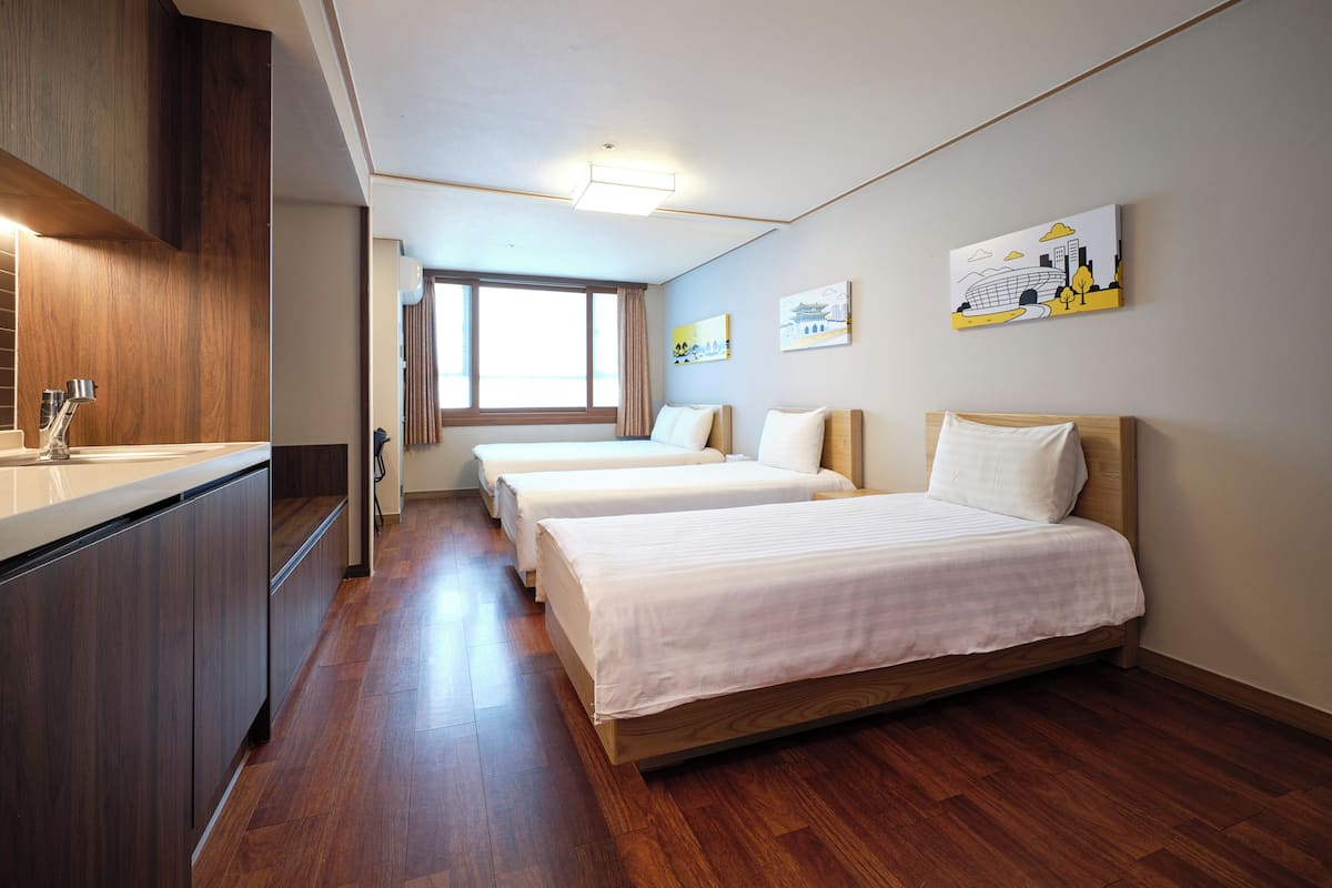 Quarto de hotel com piso de madeira, cozinha compacta, duas camas e obras de arte nas paredes.