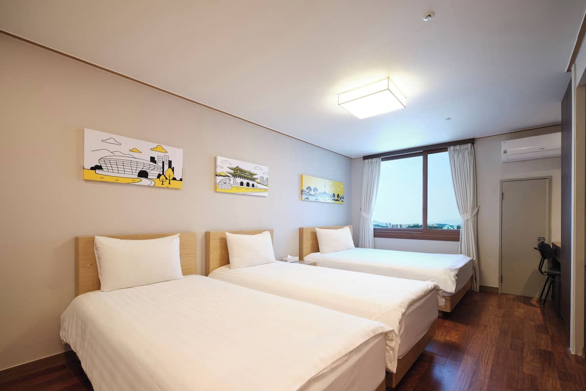 Quarto de hotel com duas camas, uma janela com cortinas e uma obra de arte na parede.