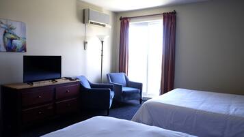 Quarto de hotel com duas camas, televisão, escrivaninha com gavetas, abajur e um quadro na parede.
