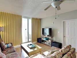 Uma sala de estar com sofá, mesa de centro, televisão e ventilador de teto.