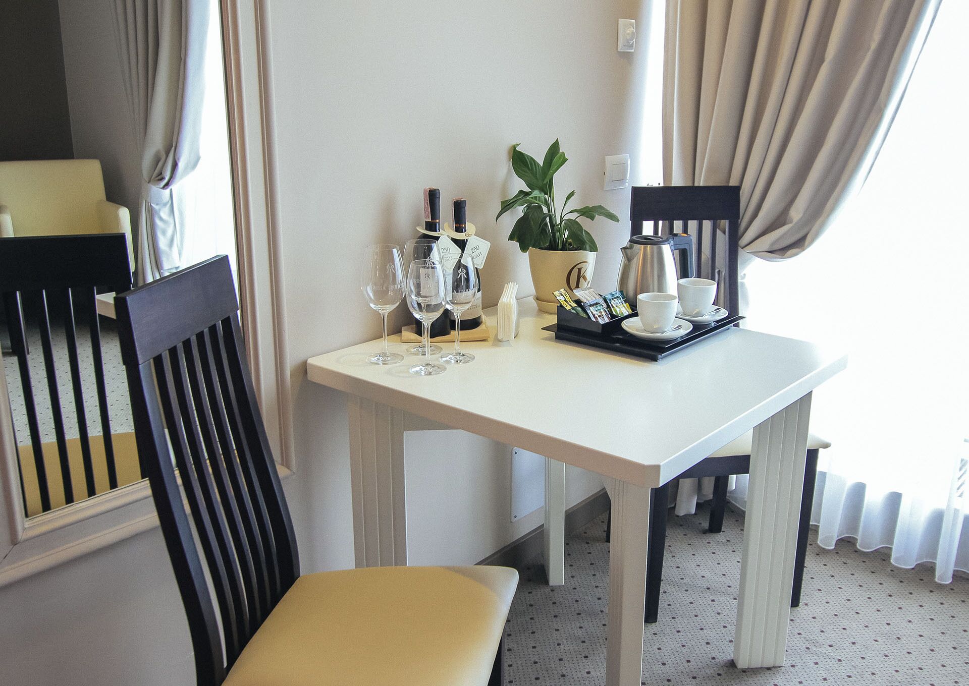 Quarto de hotel com uma mesa branca posta para o café da manhã, incluindo taças de vinho, um coador de café e uma bandeja com xícaras e pires.