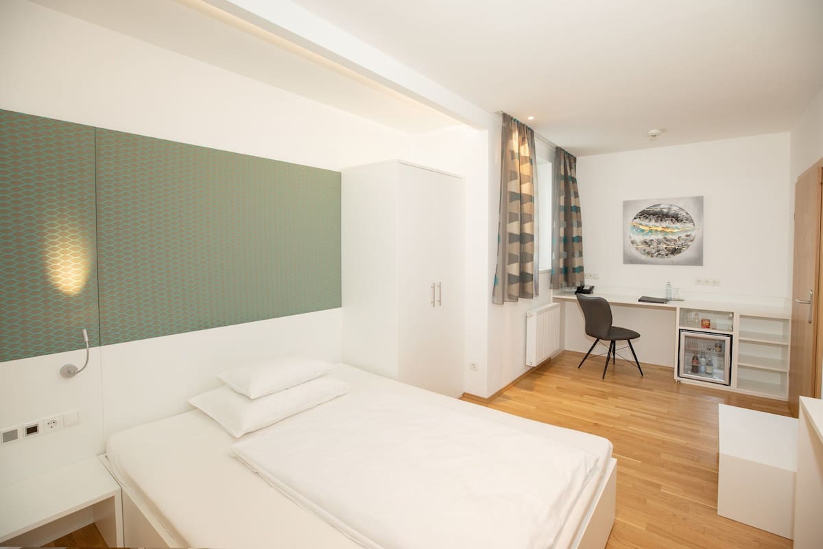 Quarto moderno com cama, escrivaninha e pequena cozinha.