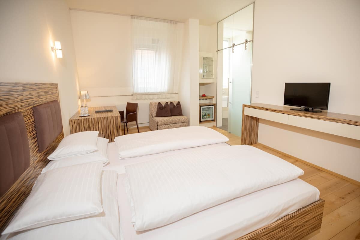 Quarto de hotel com uma cama grande, televisão, secretária com candeeiro, cadeira e guarda-roupa.