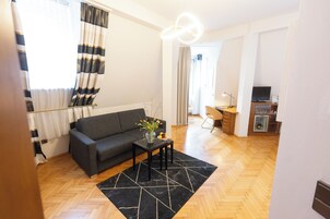 Uma sala de estar com sofá, mesa de centro com flores, televisão e escrivaninha com abajur.