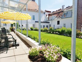 Uma área de pátio com mobiliário de jardim, guarda-sóis listrados em amarelo e um gramado bem cuidado.
