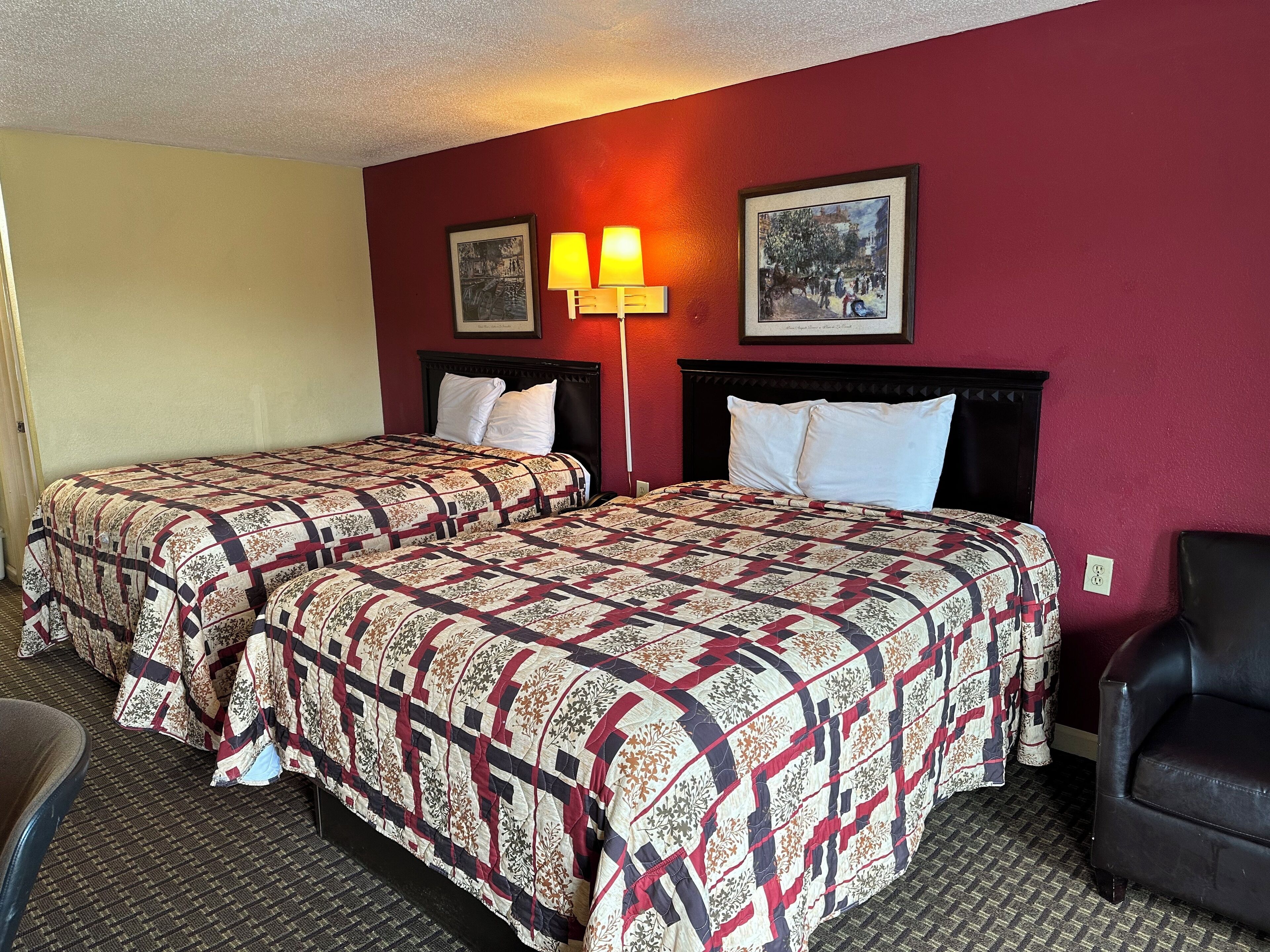 Quarto de hotel com duas camas, uma luminária e duas fotos emolduradas na parede.