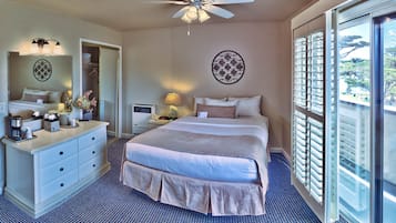 Quarto de hotel com cama grande, penteadeira, ventoinha no teto, janela com persianas e vista para o exterior.