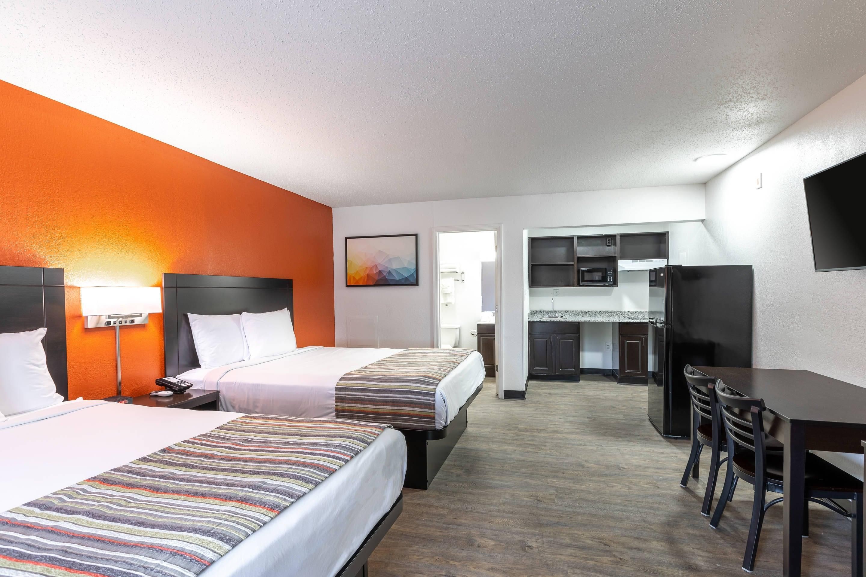 Quarto de hotel com duas camas, uma escrivaninha e uma cozinha compacta.