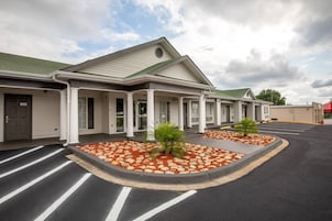 Hotel com entrada coberta, estacionamento e fileira de quartos com telhado verde.
