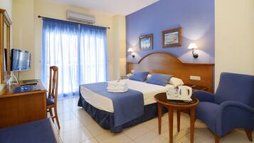 Quarto de hotel com cama, escrivaninha, cadeira, televisão e janela com cortinas.
