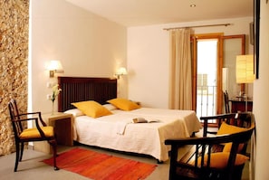 Quarto de hotel com cama, duas cadeiras, mesa de cabeceira, luminária e janela com cortinas.