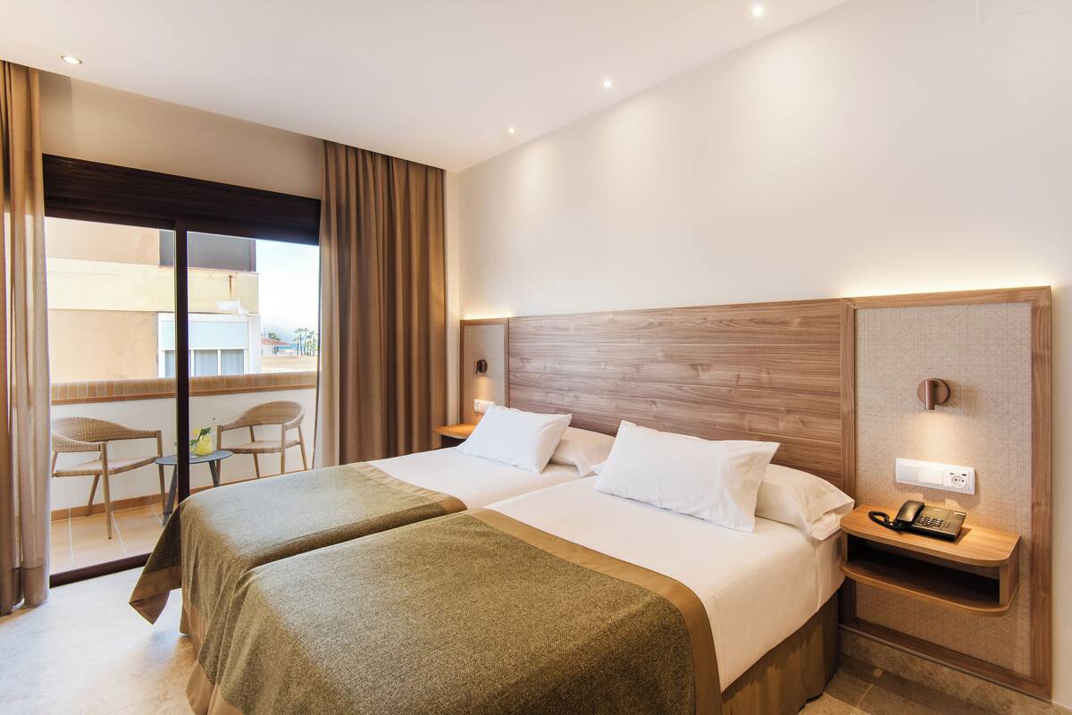 Quarto de hotel com duas camas, uma escrivaninha e uma cadeira.