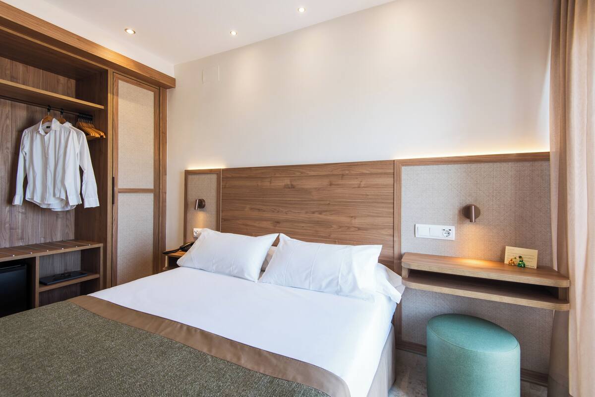 Quarto de hotel com cama grande, cabeceira de madeira, mesas de cabeceira, guarda-roupa e um pequeno espaço de estar.