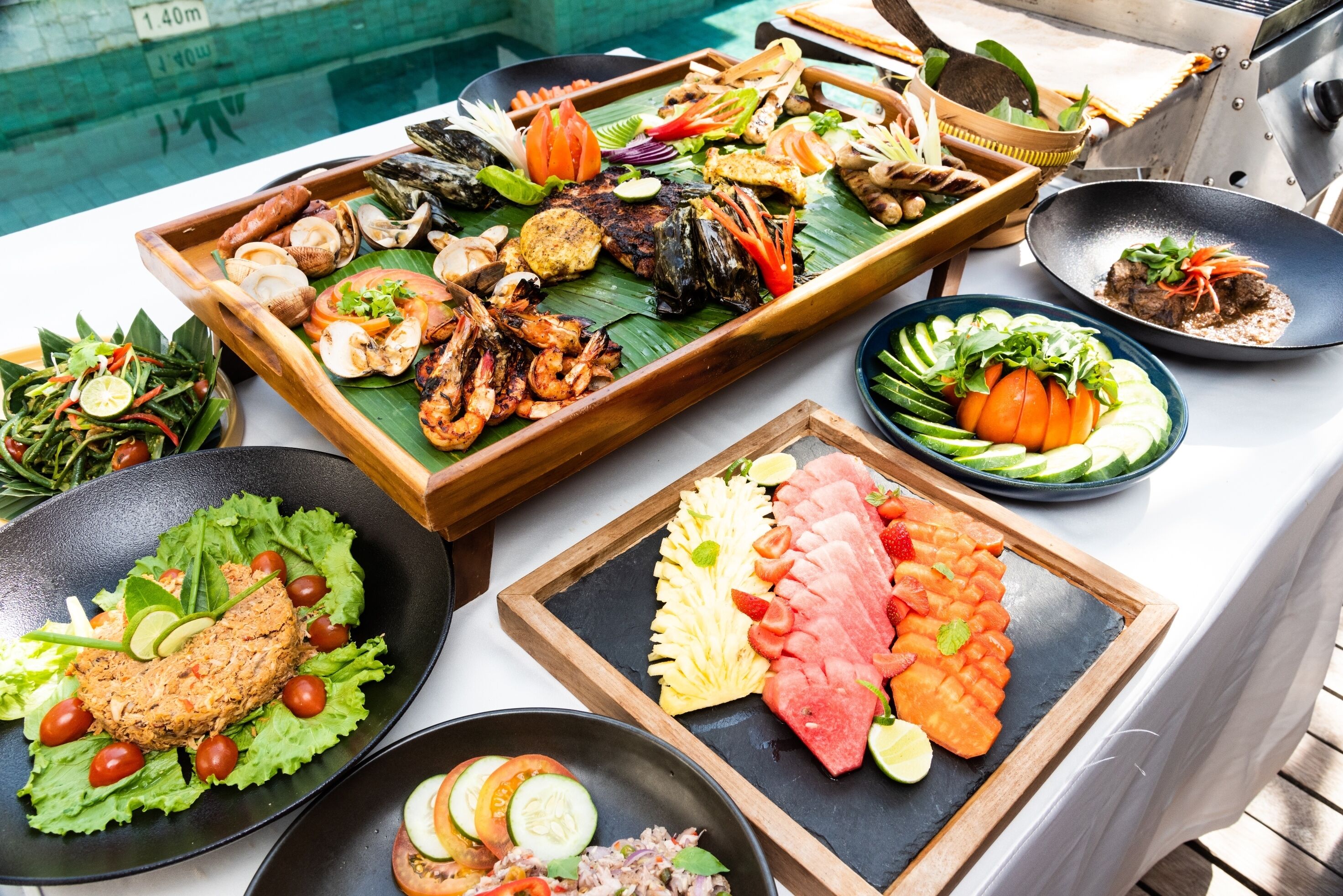 Diversos frutos do mar e saladas dispostos sobre uma mesa perto de uma piscina.