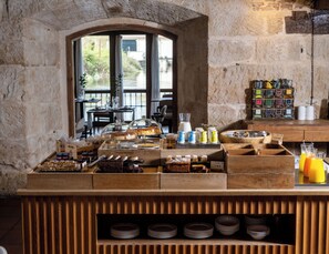 Um buffet de café da manhã com diversos pães e uma estação de café, com vista para o exterior em um cenário de parede de pedra.