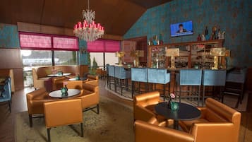 Uma área de bar com cadeiras e mesas de couro, um balcão com garrafas e uma tela de televisão.