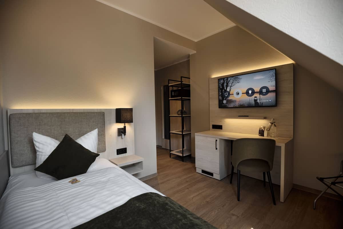 Quarto de hotel moderno com cama, escrivaninha, cadeira e televisão.