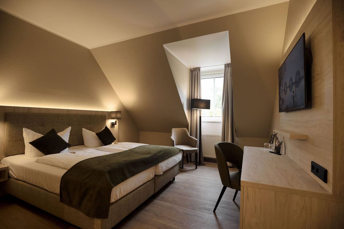 Quarto de hotel moderno com cama, escrivaninha, cadeira e uma janela grande.