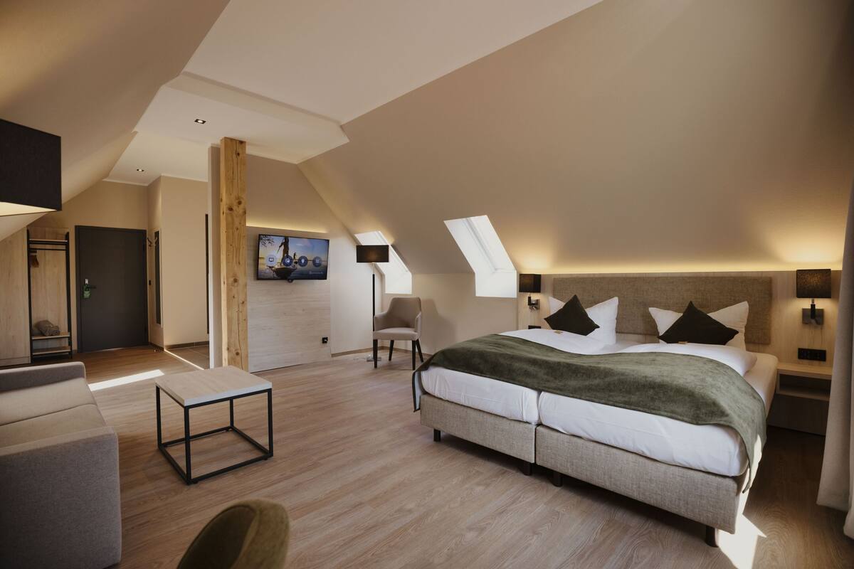 Quarto moderno com cama grande, sofá, mesa pequena e cadeira.