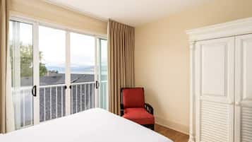 Quarto de hotel com uma cama grande, uma cadeira vermelha, um guarda-roupa e varanda com vista para a paisagem urbana.
