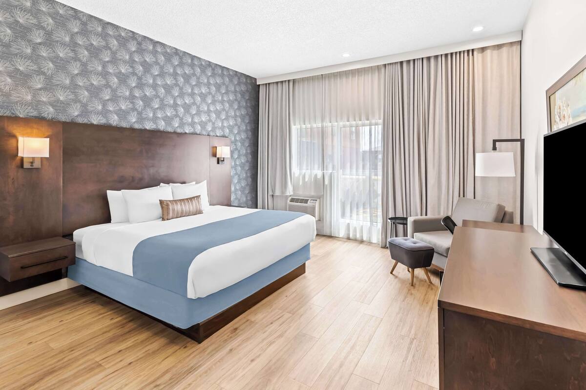 Quarto de hotel moderno com uma cama grande, uma escrivaninha, uma cadeira e uma televisão.