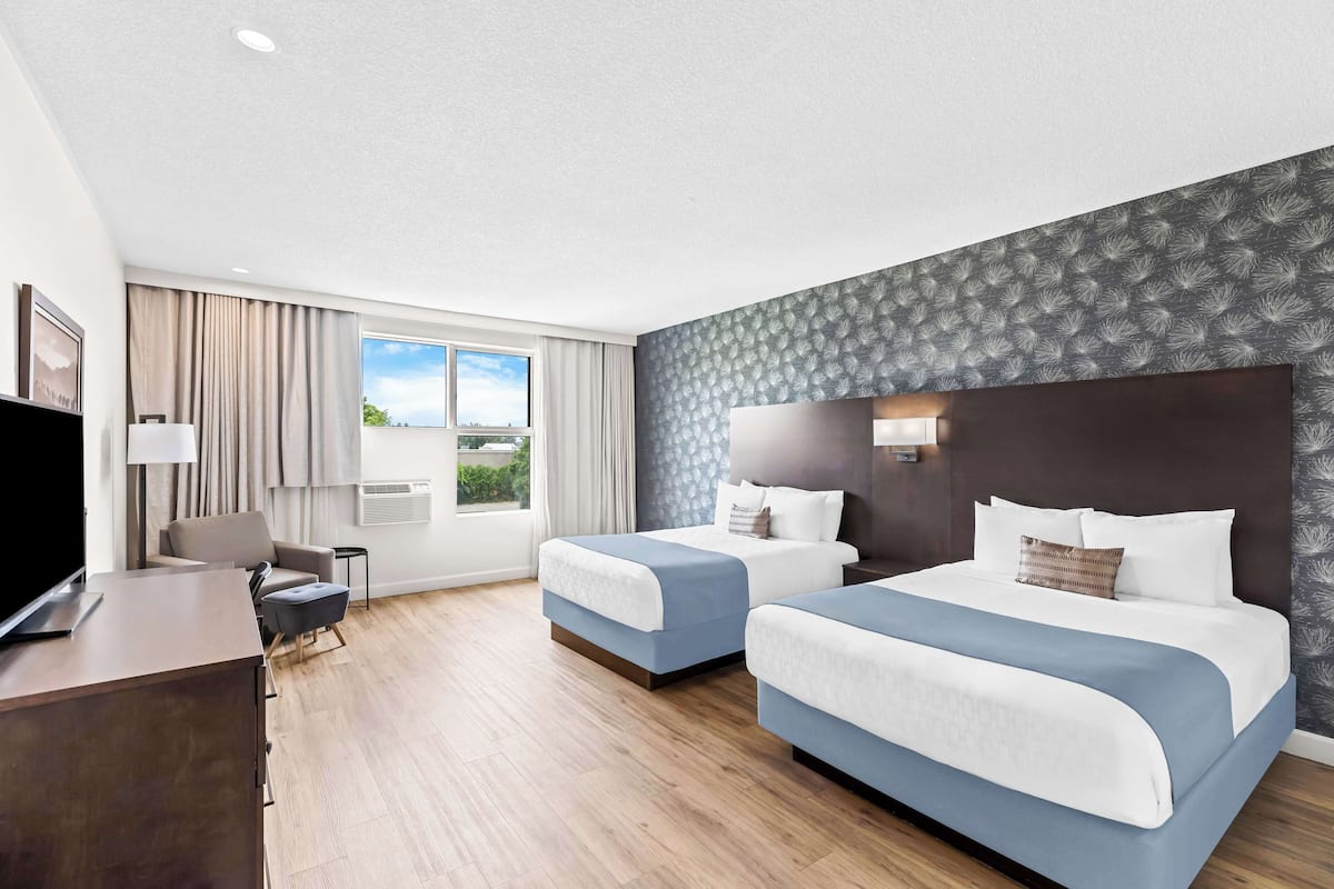 Quarto de hotel com duas camas, uma escrivaninha, televisão e janela com cortinas.