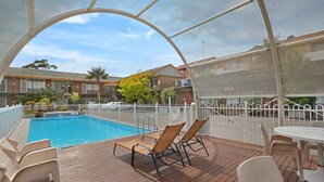 Uma área de piscina com deck de madeira, cadeiras de descanso e um espaço de estar coberto.