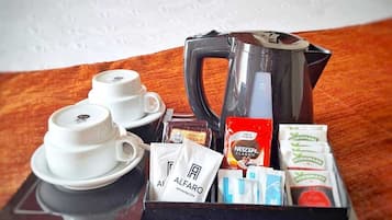 Uma bandeja com cafeteira, duas xícaras e diversos sachês de café sobre uma cama com lençóis brancos.