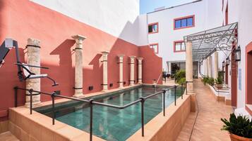Uma área de piscina com deck revestido de azulejos, colunas e um espaço coberto para sentar.