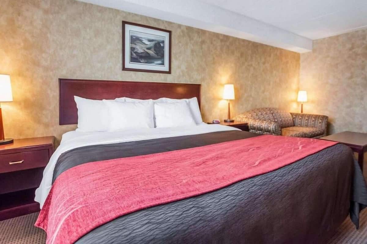 Quarto de hotel com uma cama, duas mesas de cabeceira, uma cadeira e um quadro na parede.