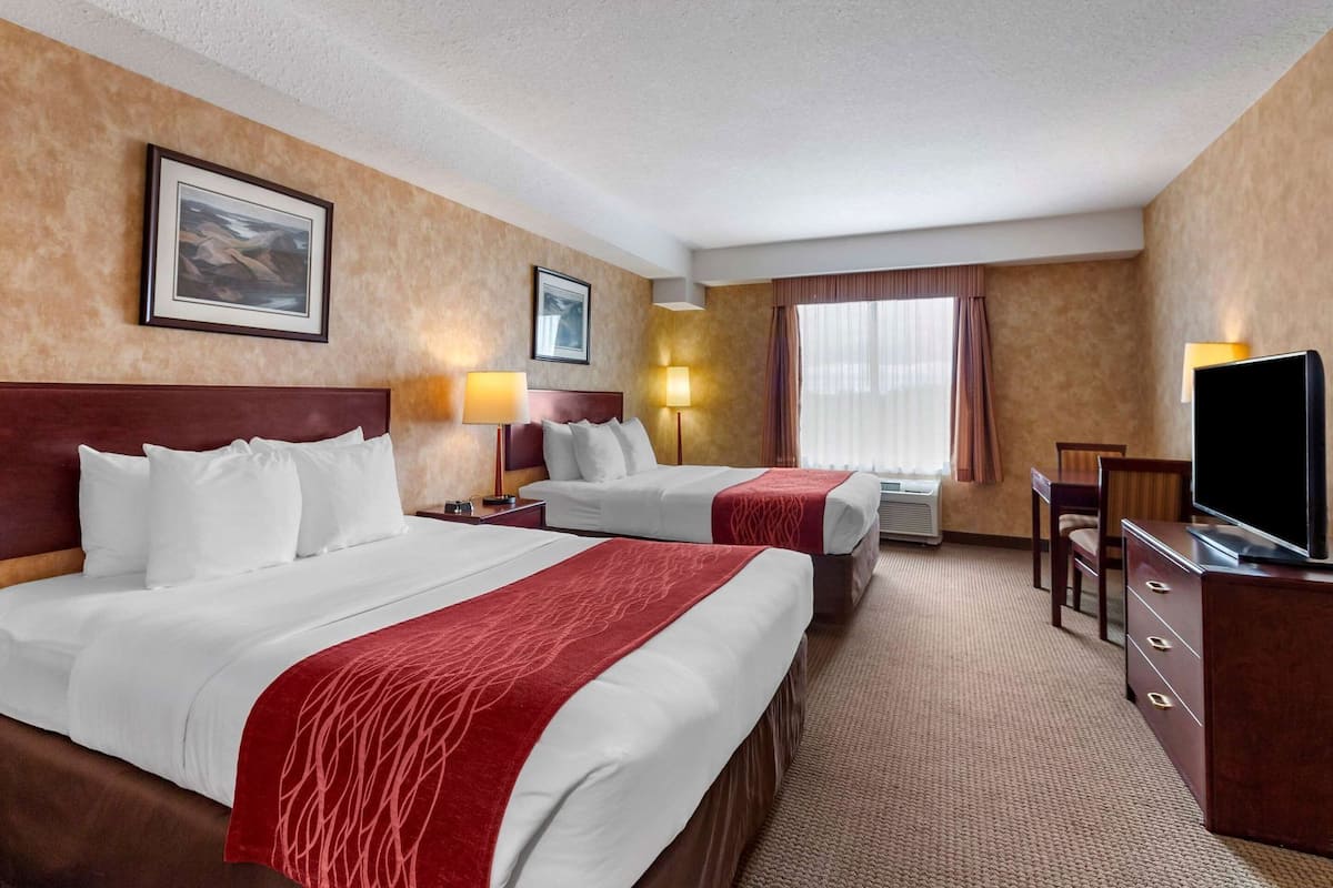Quarto de hotel com duas camas, televisão, escrivaninha e luminária.